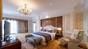 Quarto de hotel espaçoso com uma cama grande, televisão, poltrona de massagem e lustre.