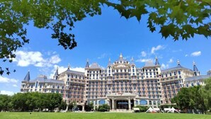 Um hotel grande e com vários andares, com fachada simétrica, inúmeras janelas e entrada central com pórtico.
