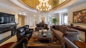 Uma sala de estar luxuosa com um candelabro, sofás de couro, uma TV de tela plana e uma lareira de mármore.