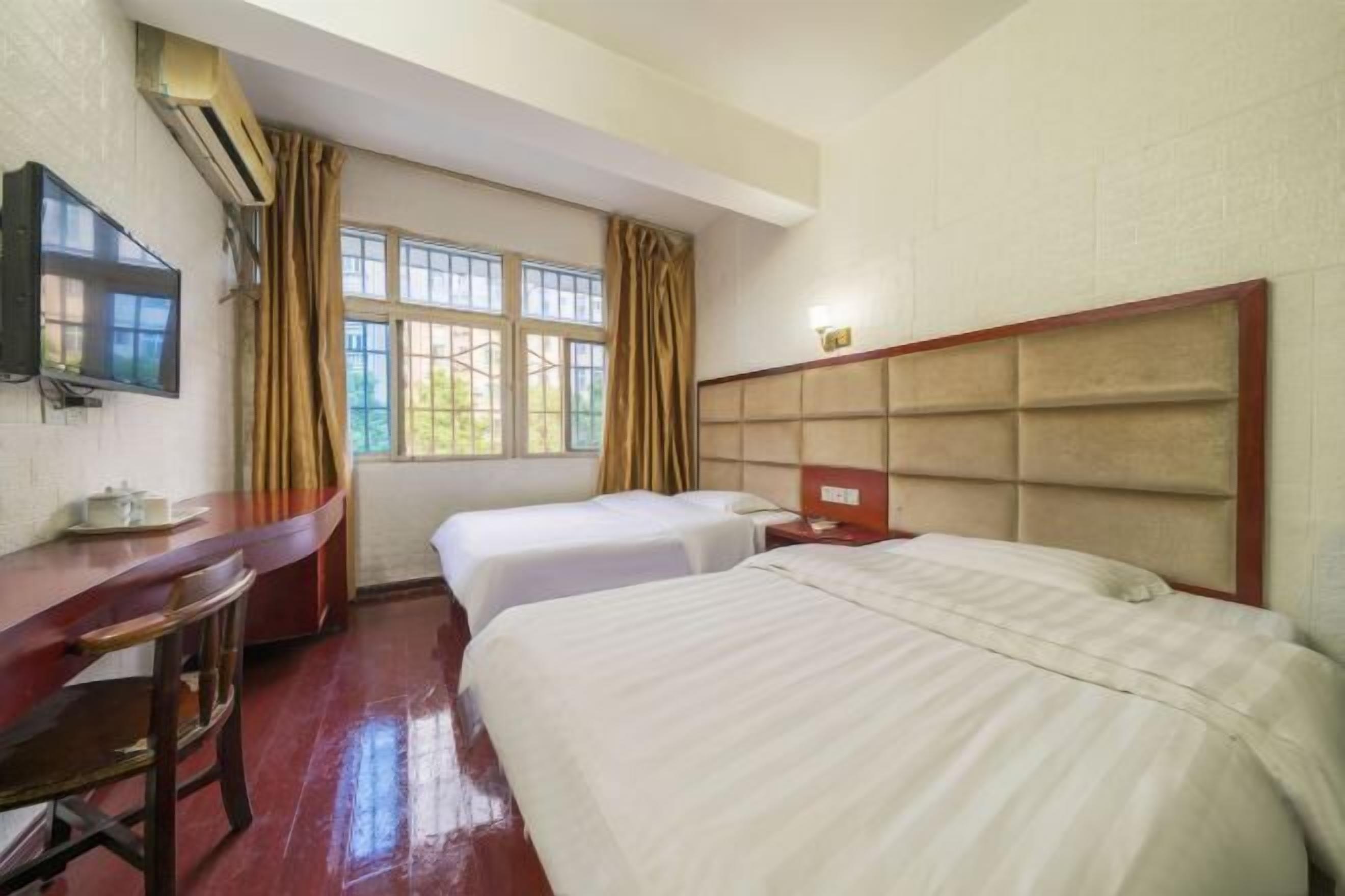 Quarto de hotel com duas camas, uma escrivaninha com cadeira, televisão e janela com cortinas.