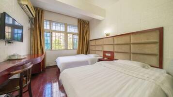 Quarto de hotel com duas camas, uma escrivaninha com cadeira, televisão e janela com cortinas.