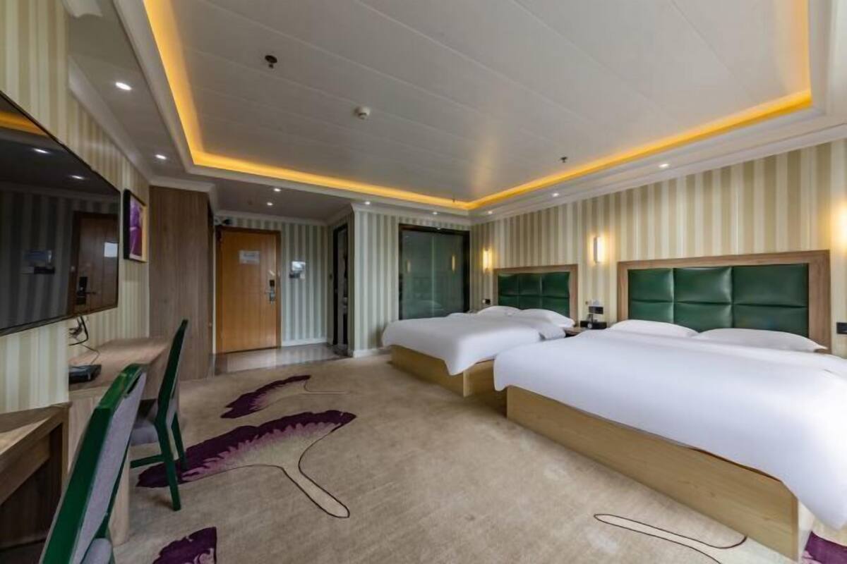 Quarto de hotel com duas camas, uma escrivaninha, uma cadeira e uma televisão.