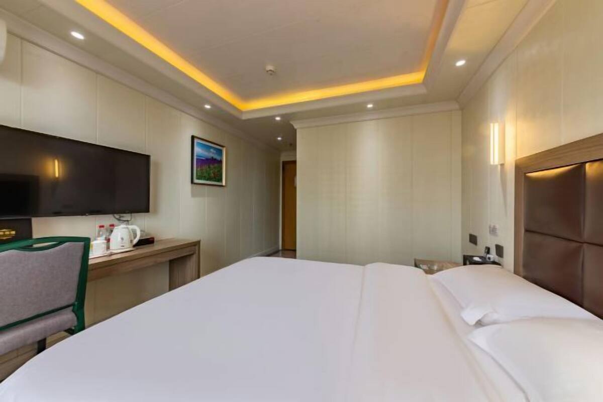 Quarto de hotel com uma cama grande, televisão de tela plana, escrivaninha com chaleira e um quadro na parede.