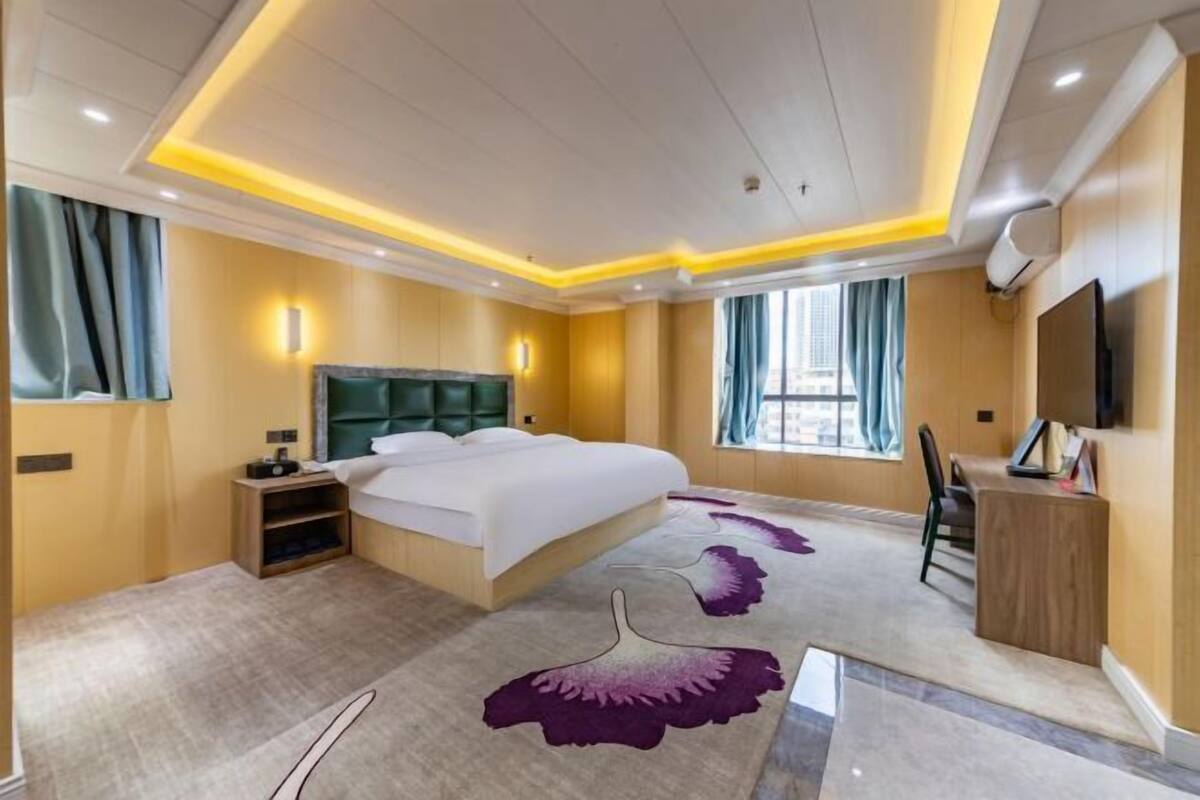 Quarto de hotel com cama, mesa de cabeceira, televisão, escrivaninha e vista para a cidade.
