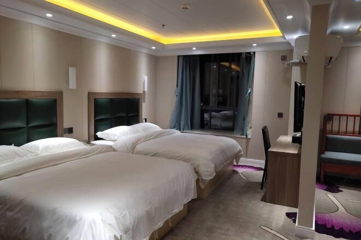 Quarto de hotel com duas camas, uma escrivaninha, uma cadeira e uma janela com cortinas.