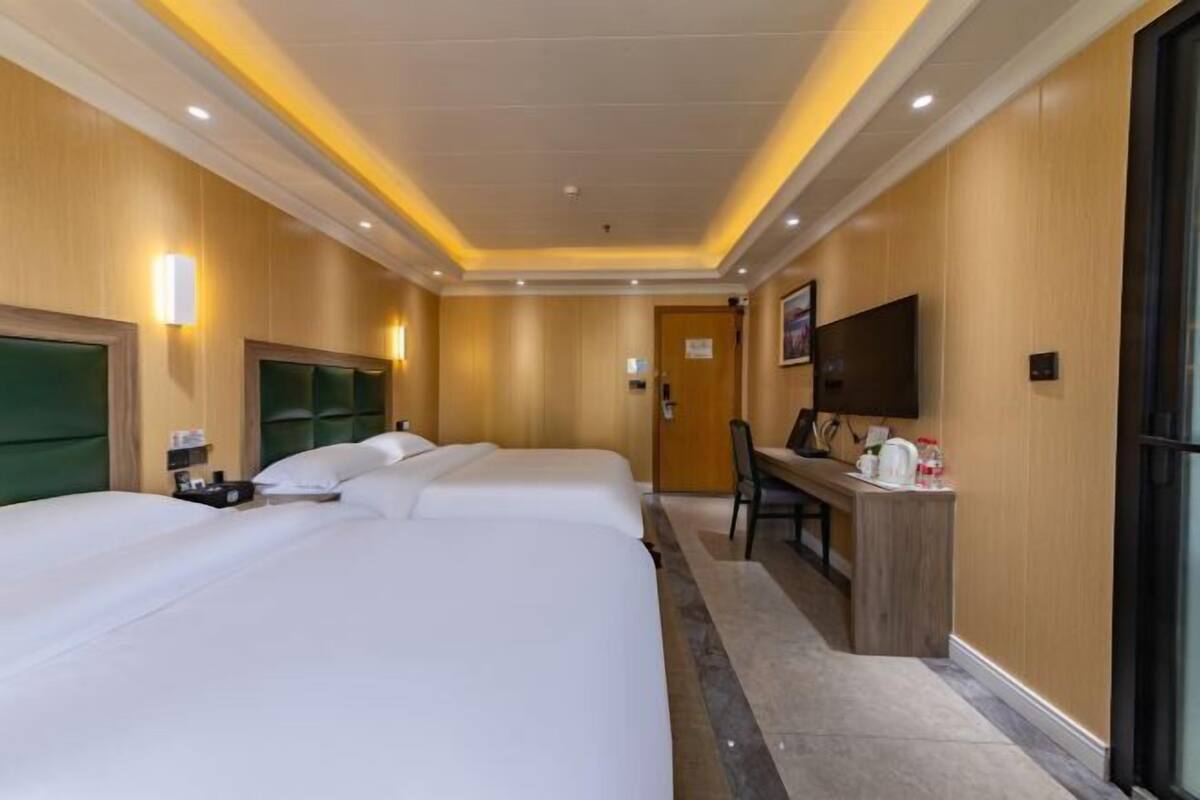 Quarto de hotel com duas camas, uma escrivaninha, uma cadeira, uma televisão e uma porta.