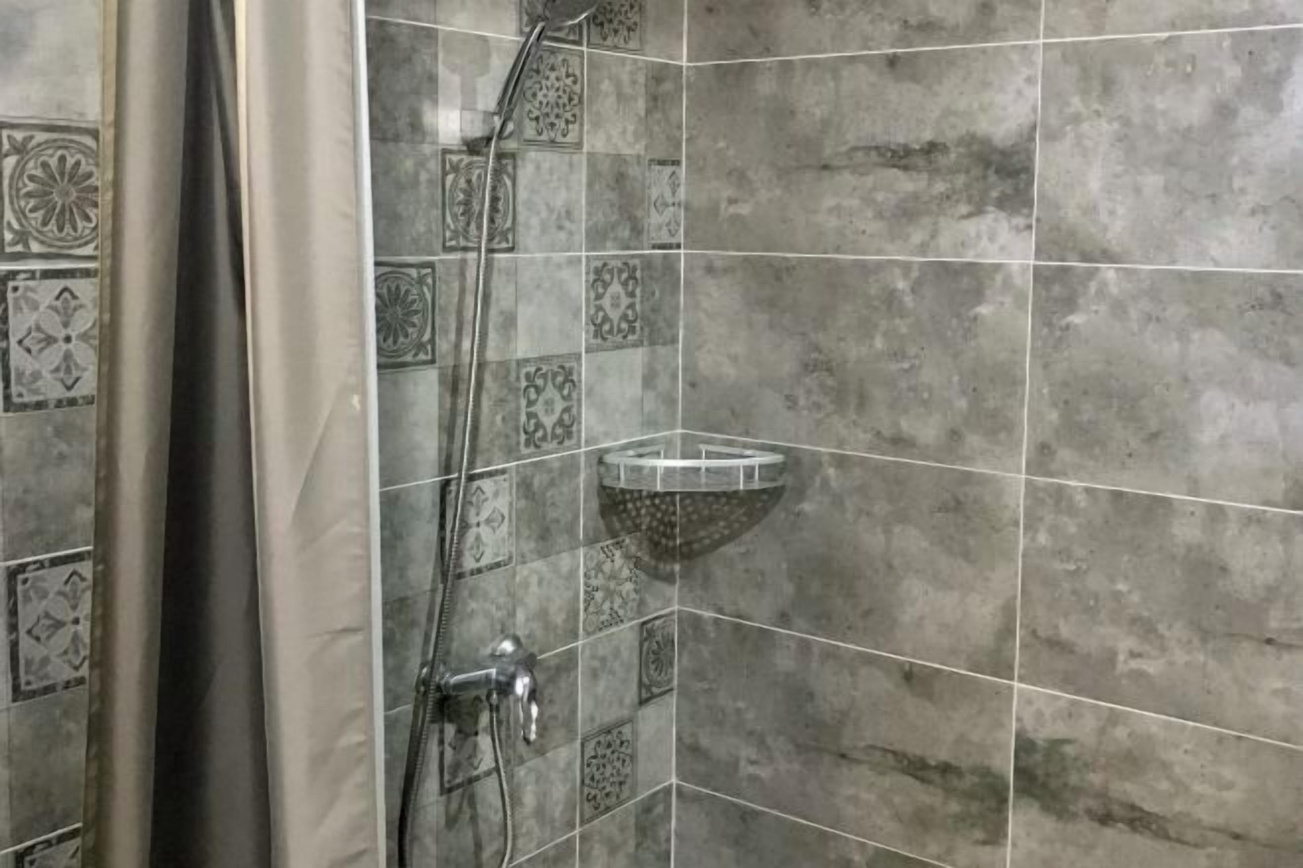 Área de duche com azulejos estampados, um chuveiro e um lavatório no canto.