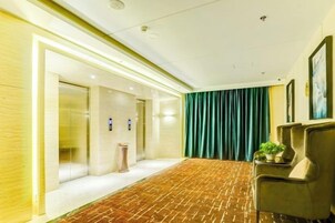 Um saguão de hotel com piso carpete, balcão de recepção, cortina verde e quadro emoldurado na parede.