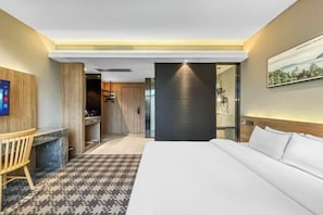 Quarto de hotel moderno com uma cama grande, uma escrivaninha e uma pequena cozinha equipada.