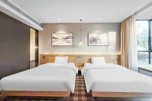 Quarto de hotel com duas camas, uma janela grande com cortinas e duas imagens emolduradas na parede.