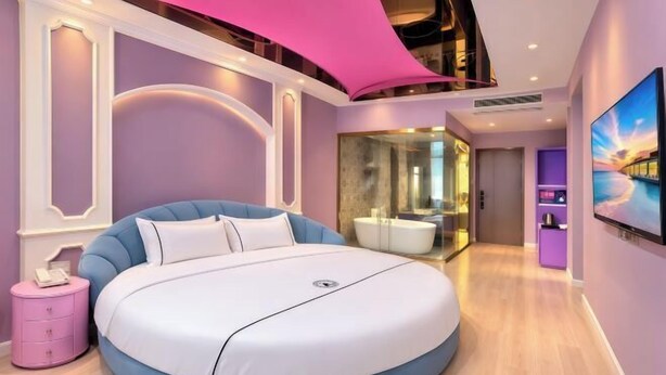 Um quarto moderno com uma cama circular, uma parede de destaque rosa e uma janela grande.