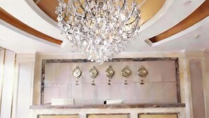 Um hall com um candelabro, um relógio na parede e um balcão de recepção.