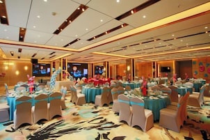 Salão de banquetes com mesas redondas, cadeiras e palco.