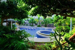 Área de piscina cercada por vegetação exuberante, com um gazebo e um pequeno edifício ao fundo.