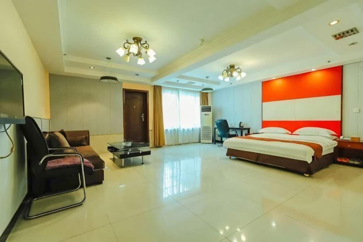 Quarto de hotel com cama, secretária, cadeira, televisão e sofá.
