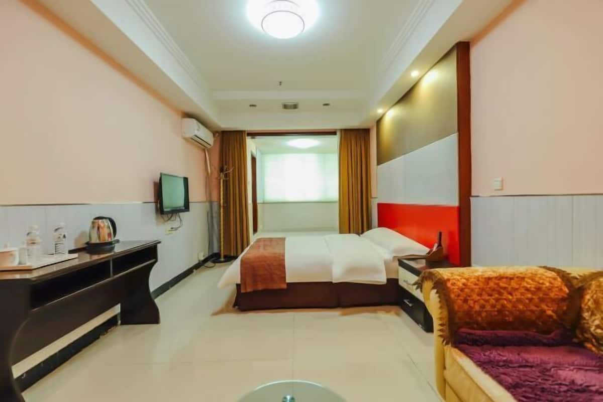 Quarto de hotel com cama, escrivaninha, televisão e sofá.