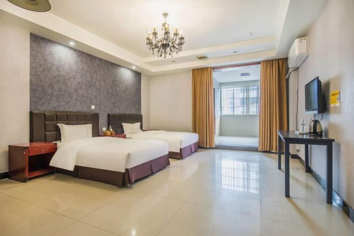 Quarto de hotel com duas camas, televisão, secretária e um candelabro.