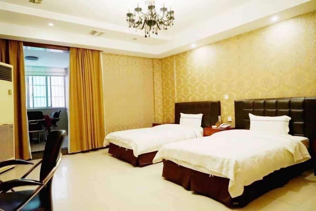 Quarto de hotel com duas camas, um candelabro, uma escrivaninha e uma cadeira.