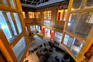 Um interior em vários níveis, com arquitetura de madeira tradicional, diversas áreas de estar e pilares vermelhos.