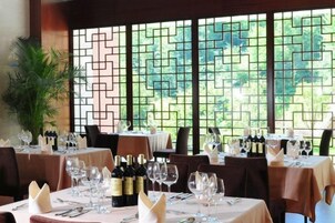 Restaurante com mesas preparadas para refeições, oferecendo vista através de uma janela com padrão geométrico.