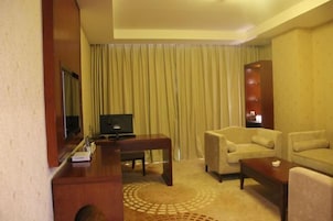 Quarto de hotel com televisão, mesa de escritório, dois sofás, mesa de centro e tapete estampado.