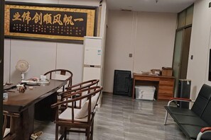 Sala de conferências com mesa de madeira, cadeiras, quadro branco e um frigorífico pequeno.