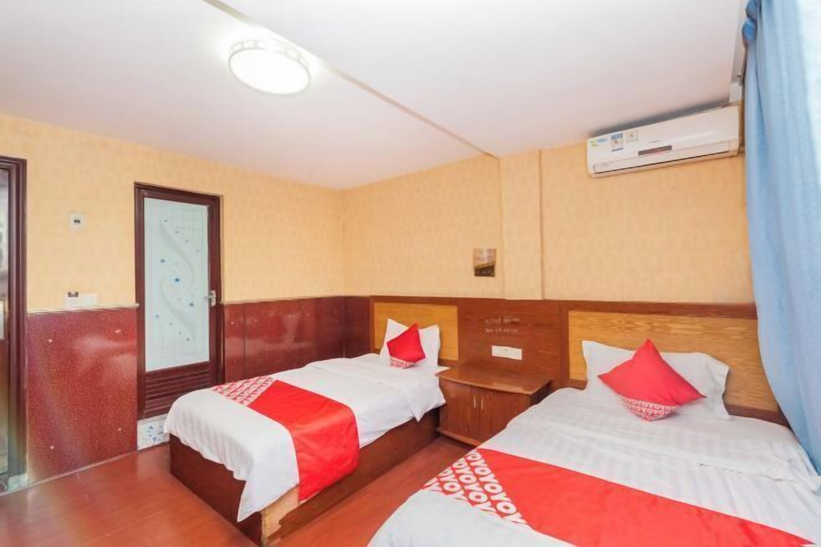Quarto de hotel com duas camas, cabeceiras de madeira, uma luminária no teto, aparelho de ar condicionado e uma porta com um mapa.