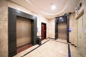 Um hall de hotel com piso de mármore, balcão de recepção e três elevadores.