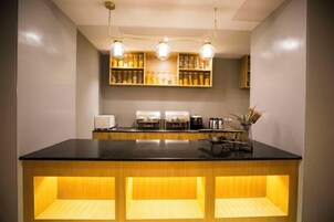 Área de bar com bancada preta, prateleiras de madeira e máquina de café.