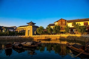 Um edifício tradicional com uma torre, um pátio com barcos e um rio.
