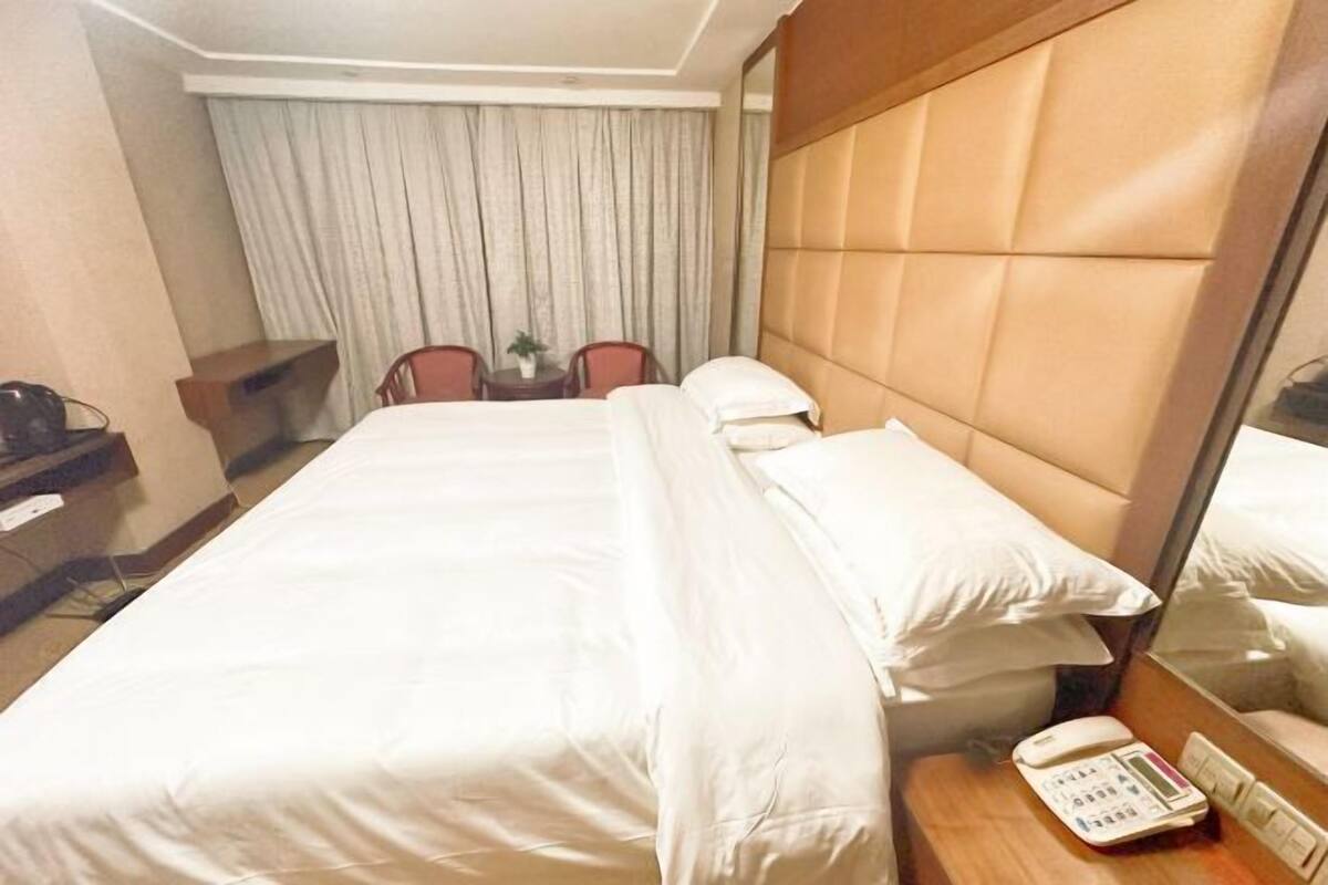 Quarto de hotel com uma cama grande, um telefone ao lado da cama e um espelho.