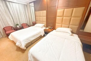 Quarto de hotel com duas camas, uma pequena mesa com uma planta, uma cadeira e uma mesa de cabeceira com um telefone.