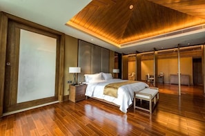 Quarto amplo com cama grande, piso de madeira, teto com design em ripas de madeira e porta deslizante.