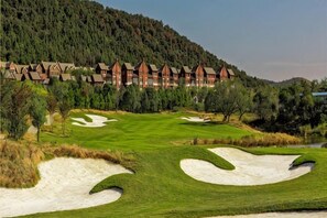 Um campo de golfe com bunkers e uma hospedaria ao fundo.