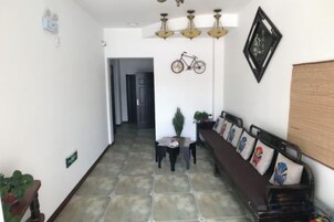 Um corredor com piso de pedra, um banco com almofadas, uma pequena mesa com uma planta e uma bicicleta fixada na parede.