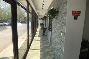 Um corredor com parede de pedra, plantas em vasos e placa indicando área de serviço 24 horas.