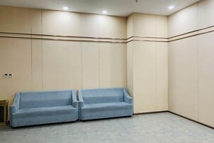 Um quarto com sofá azul claro, paredes bege e piso de azulejos.