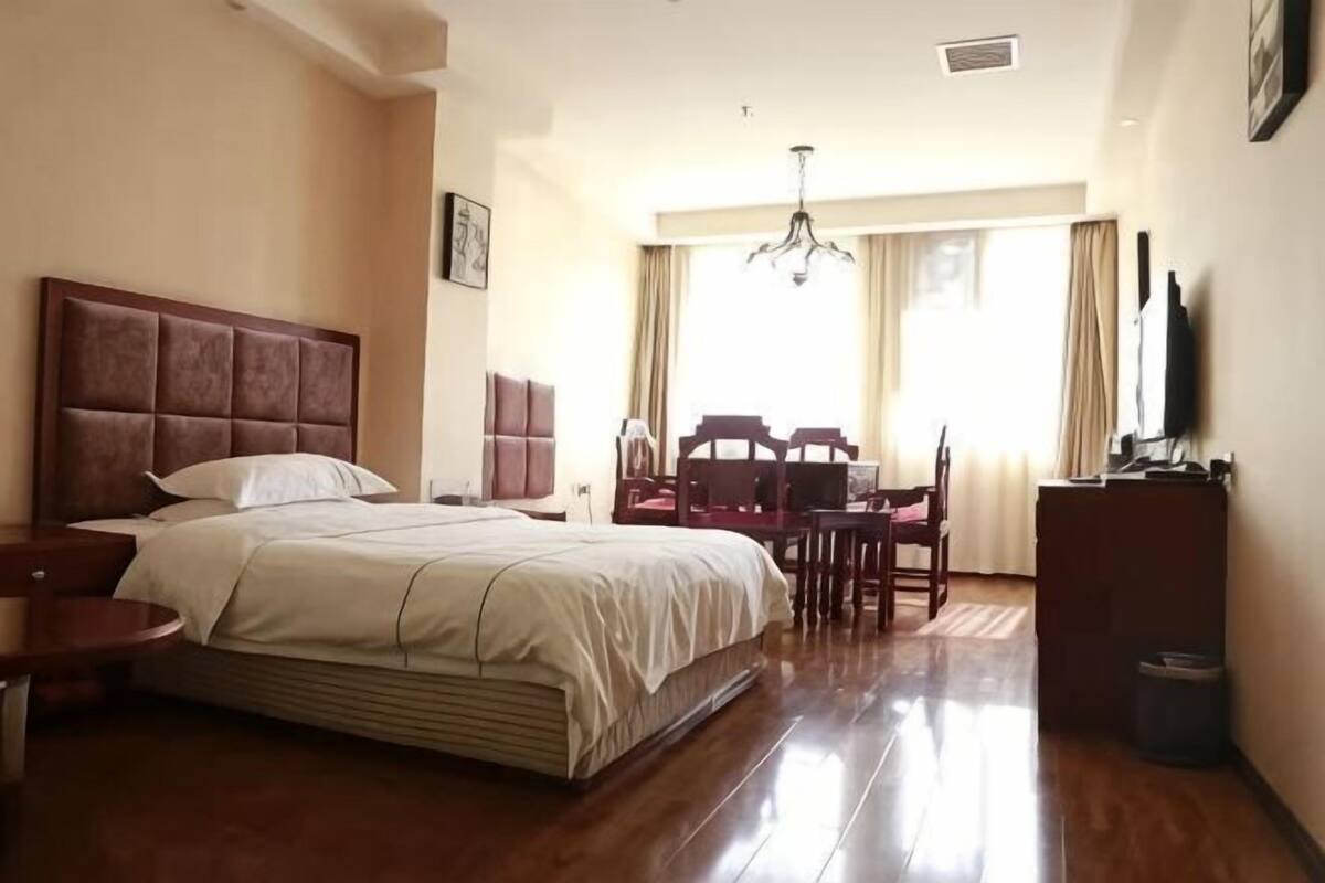 Quarto de hotel com cama, escrivaninha, cadeira, televisão e janela com cortinas.