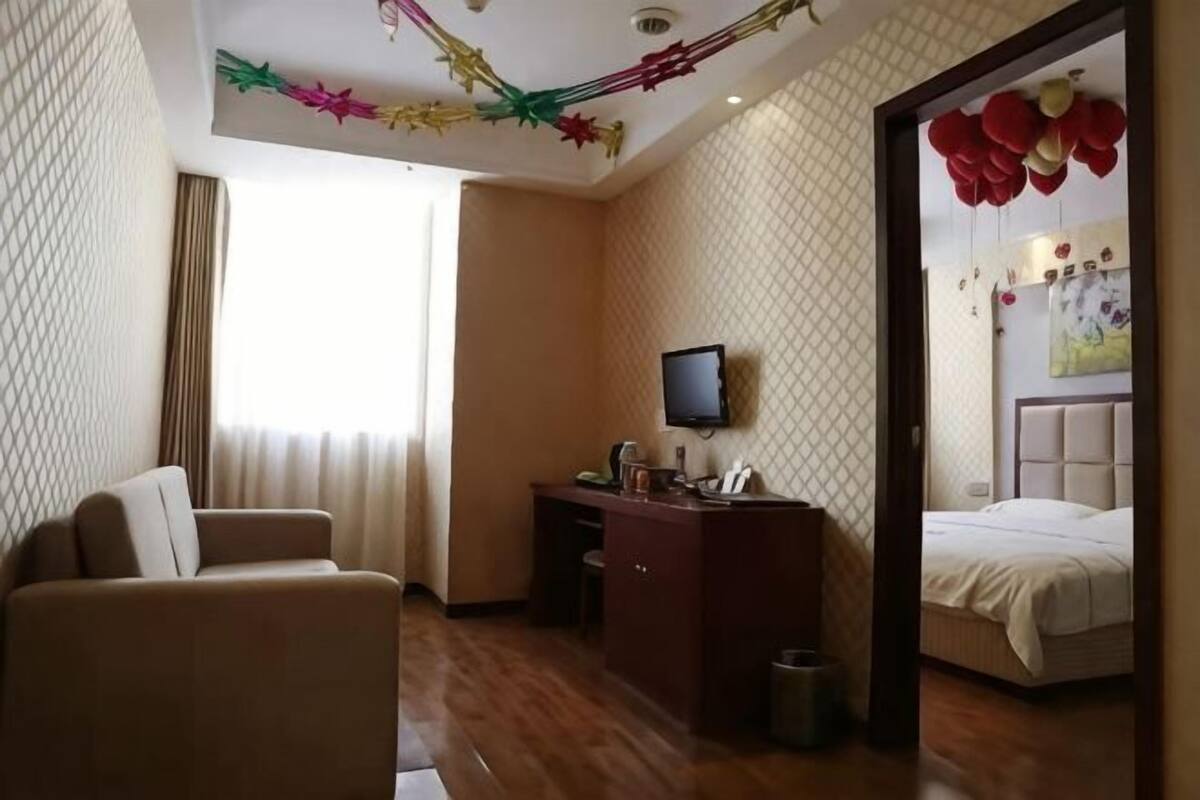 Quarto de hotel com sofá, televisão, cama e pequena escrivaninha.
