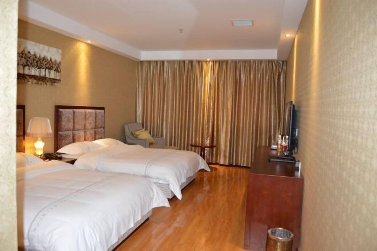 Quarto de hotel com duas camas, uma poltrona, uma escrivaninha e uma televisão.