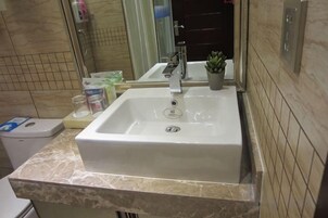 Casa de banho com lavatório branco, espelho e uma pequena planta num vaso sobre a bancada.