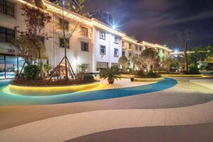 Pátio de hotel com piscina, plantas em vasos e fachada de edifício bem iluminada.