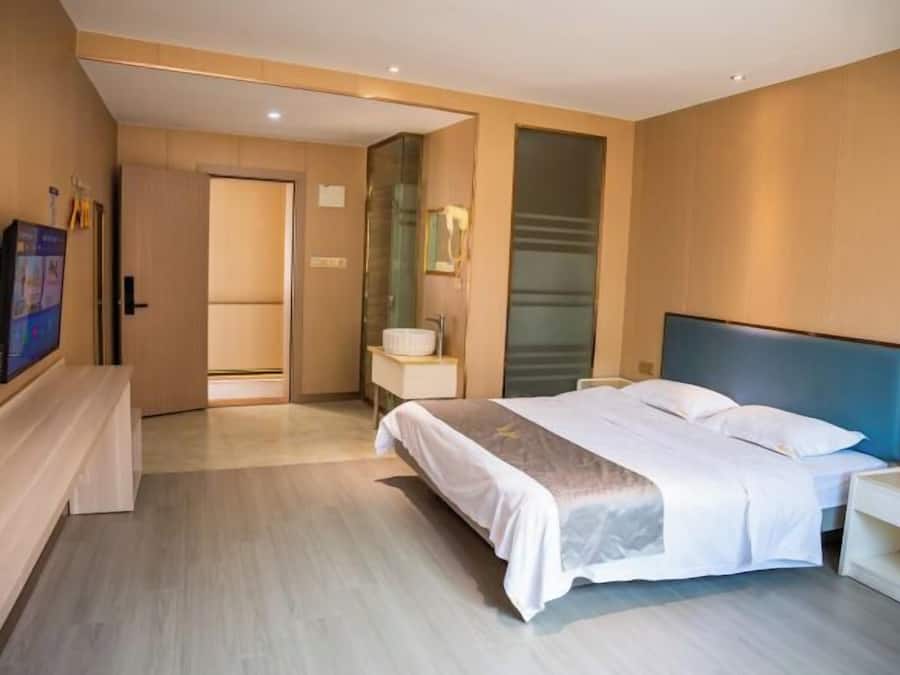 Quarto de hotel moderno com uma cama grande, mesas de cabeceira, televisão e banheiro visível através de uma porta aberta.