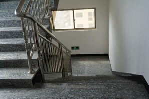 Uma escada com corrimãos de metal, piso revestido de carpete e uma janela com persianas.