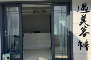 Entrada de hotel com porta de vidro deslizante, balcão de recepção e placa com caracteres chineses.