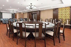 Uma sala de conferências com uma mesa redonda, cadeiras, um candelabro e um papel de parede estampado.
