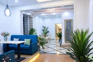 Um hall moderno com um sofá azul, uma mesa de centro e plantas em vasos.