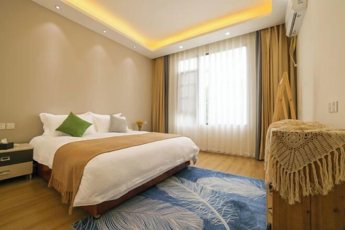 Quarto moderno com uma cama grande, uma mesa de cabeceira de madeira, um criado-mudo e uma janela ampla com cortinas.