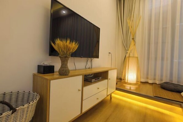 Uma sala de estar moderna com uma TV de tela plana na parede, um armário de madeira com gavetas, uma cesta de vime e um abajur.