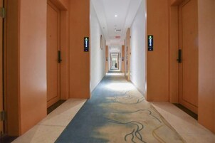 Corredor de hotel com portas em ambos os lados, piso coberto de carpete e placas de sinalização nas paredes.